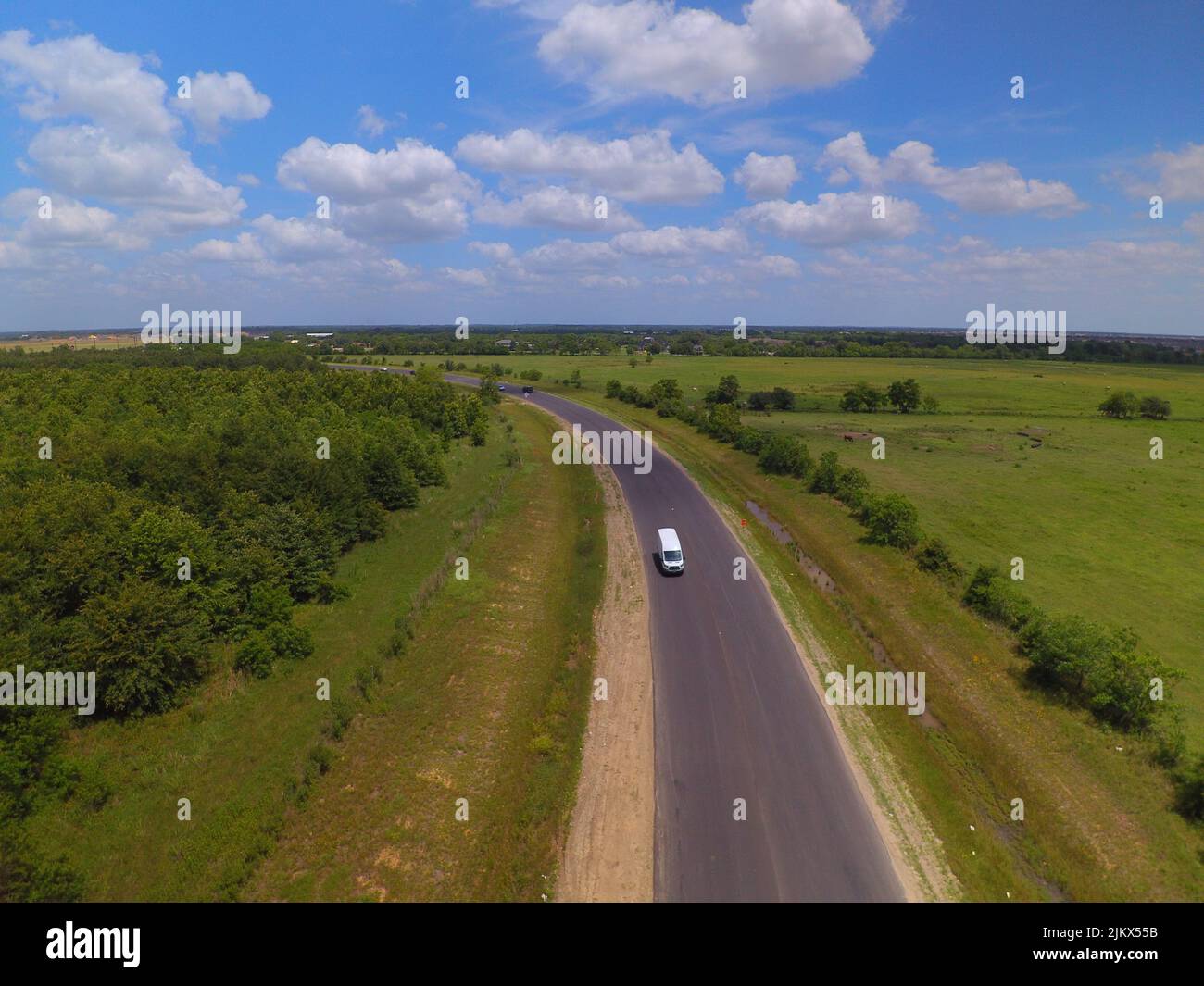 An aerial shot of a car on a road in a forest under the cloudy skies ...