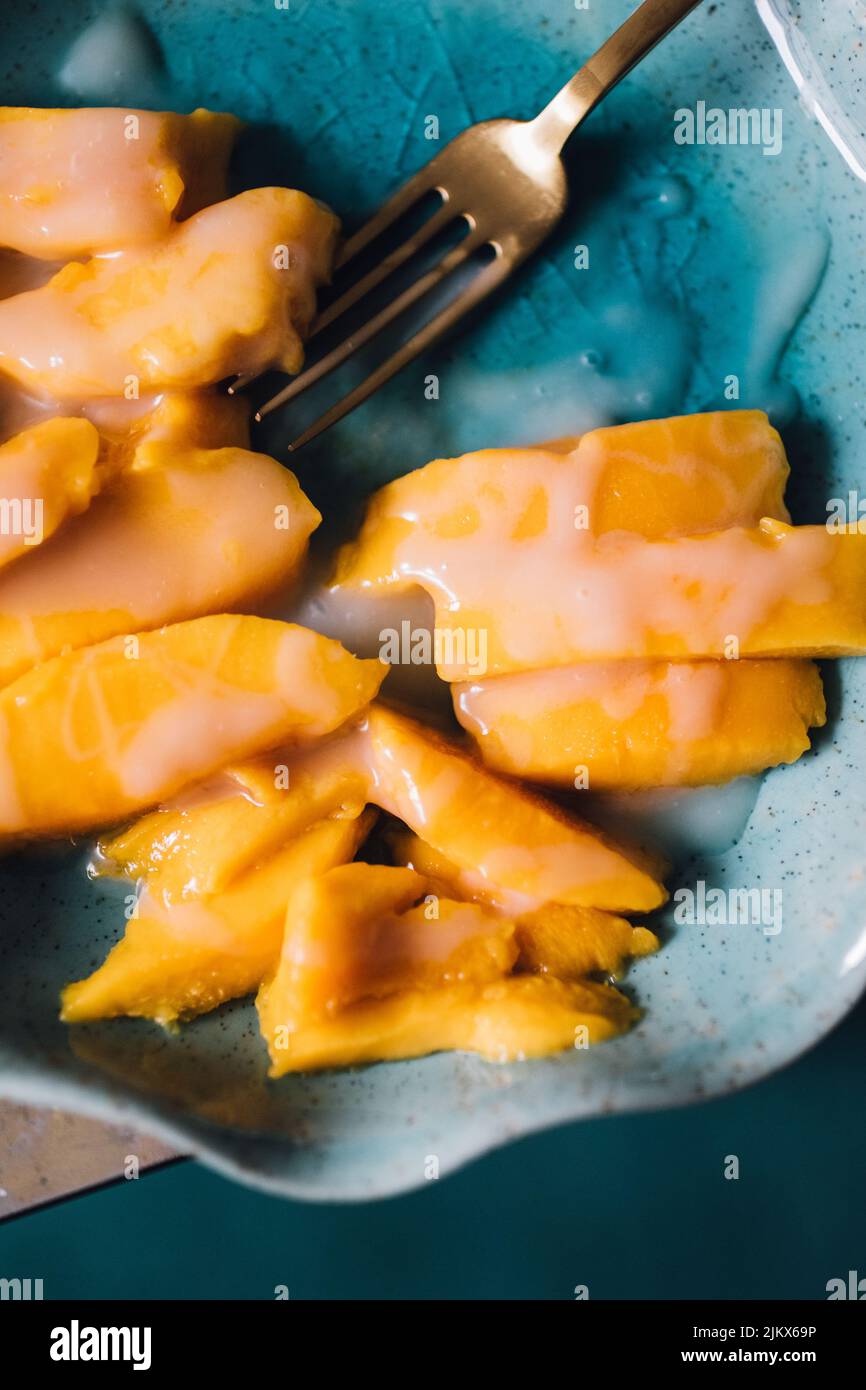 Yellow Mango slices with condensed coconut milk on teal plate with gold ...