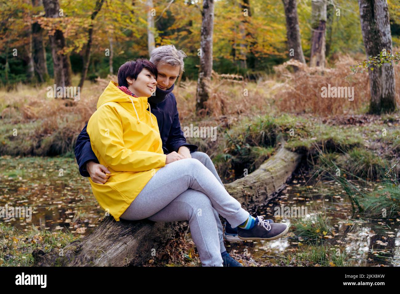 Couple in love sitting on a fallen tree near river, looking at the ...