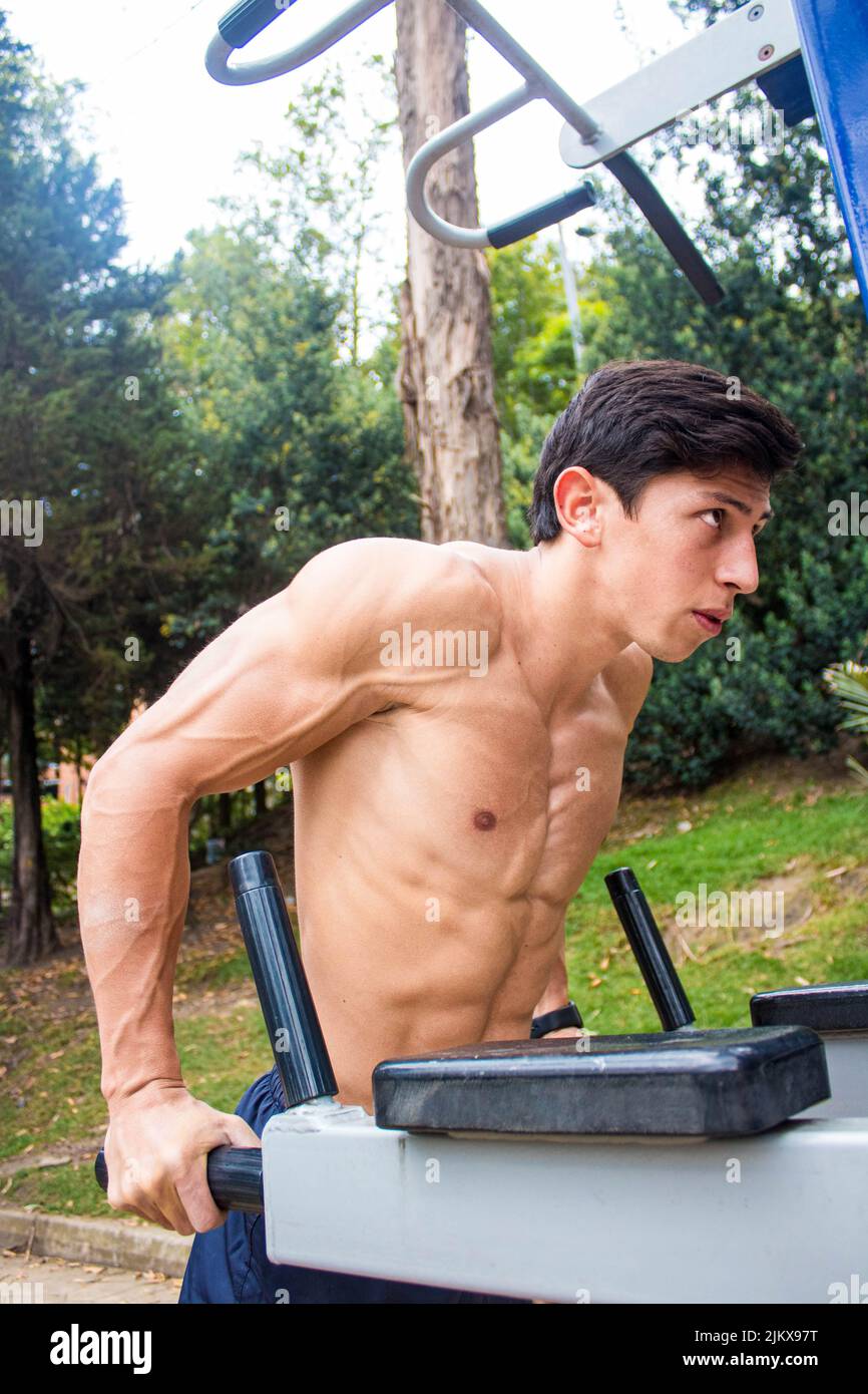 A vertical closeup of a Hispanic male athlete doing gymnastics outdoors ...