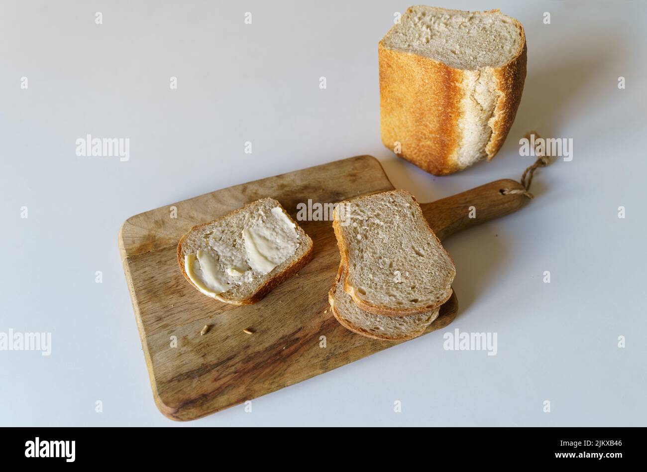 Sliced pieces of bread lie on a wooden board, one piece is buttered ...