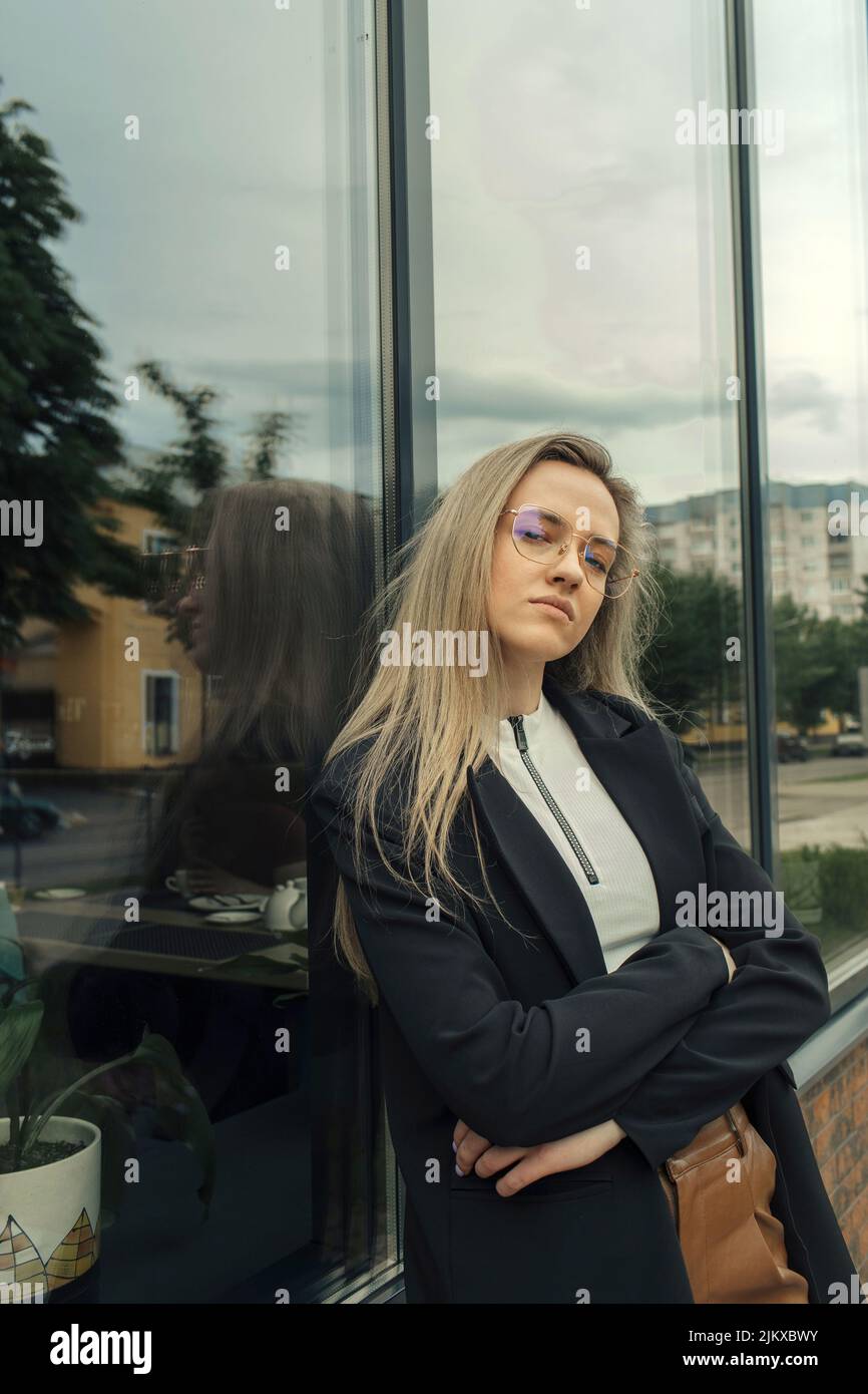 A beautiful woman in glasses stands leaning against the window of a ...