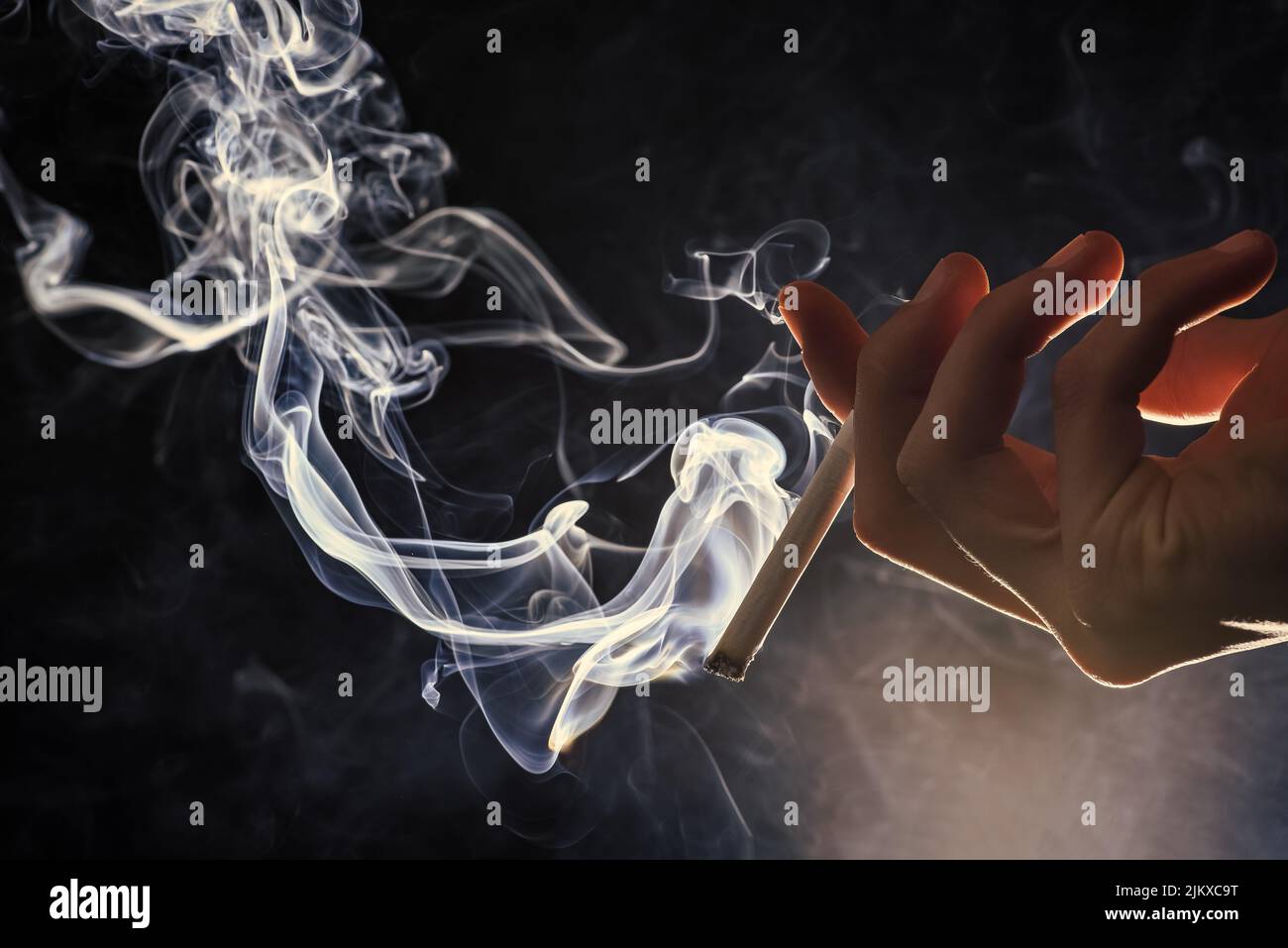 Male hand hold burning cigarette with swirl of smoke dark background ...
