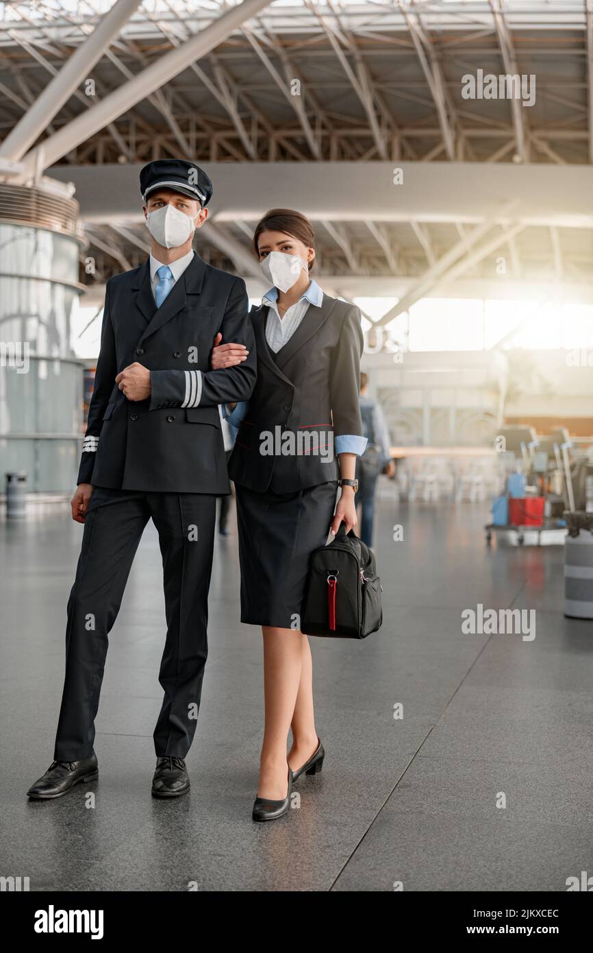Stewardess and pilot in protective face masks walking in the terminal ...