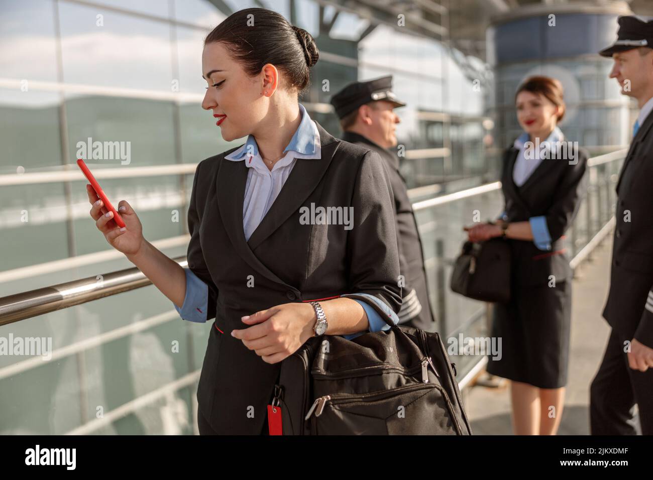 Smiling stewardess holding smartphone while standing with colleagues ...