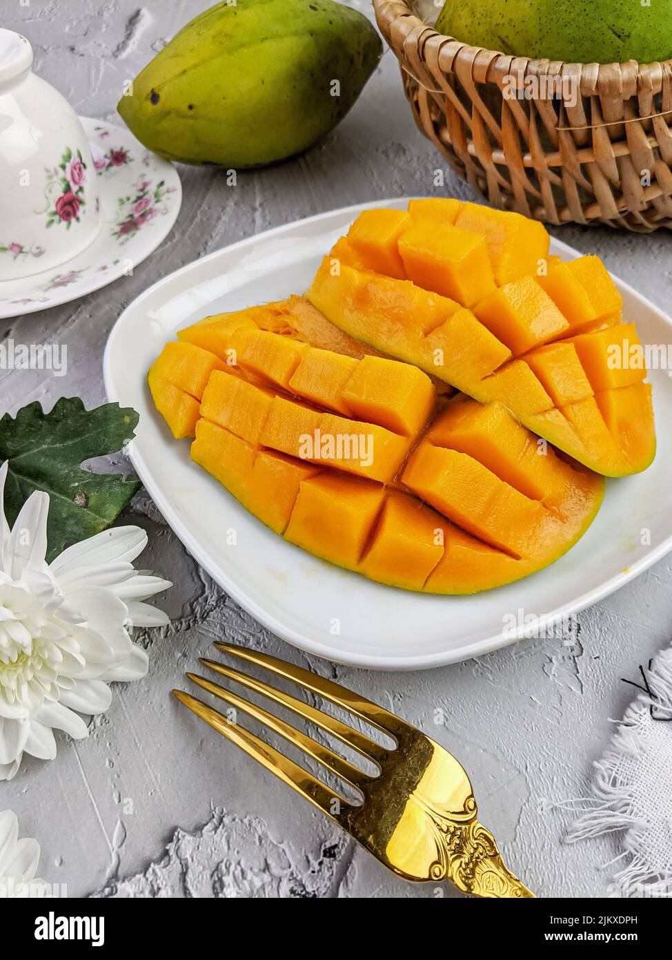 A peeled mango on a white plate with a basket full of mangos and a ...