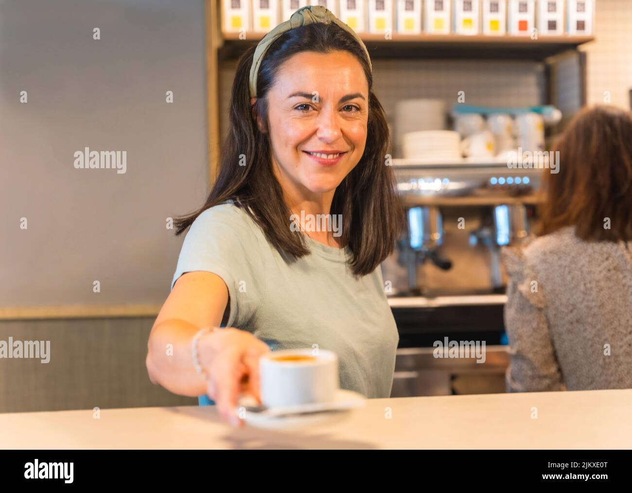 Female cafe owner with a latte in hand, offering the coffee to the ...