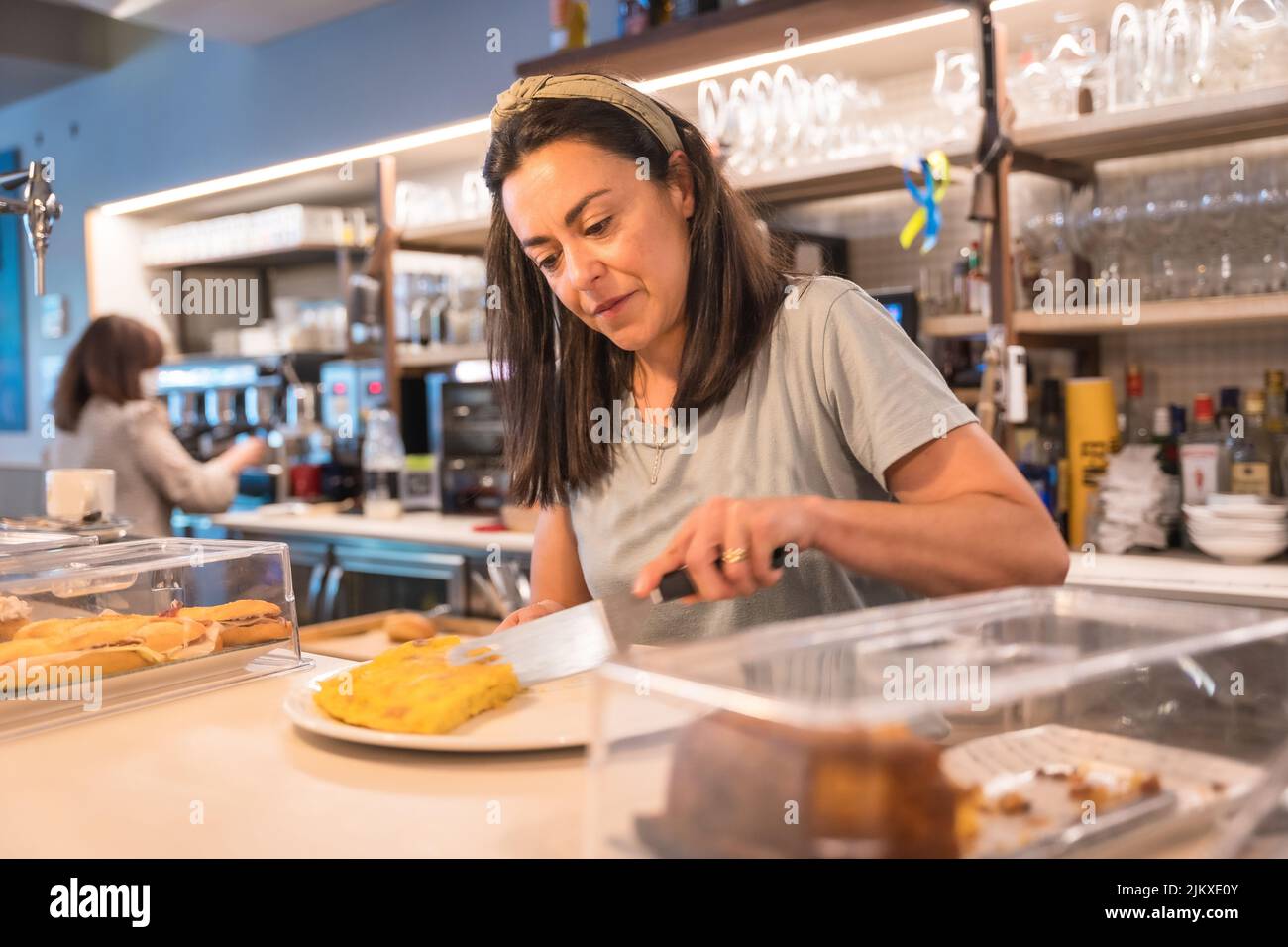 Female cafe owner cutting a snack for the customer to take with the ...