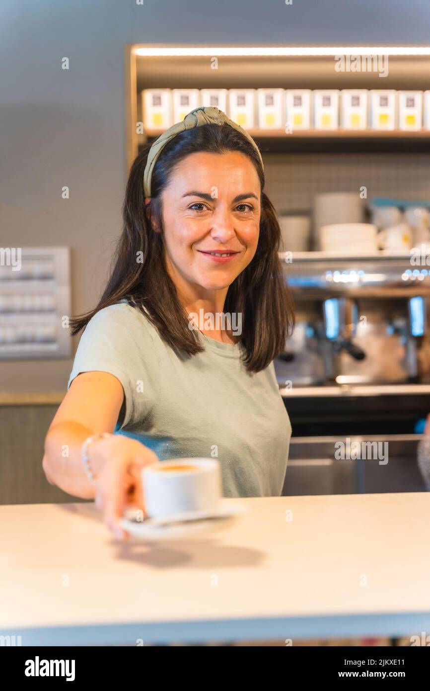 Female cafe owner with a latte in hand, offering the coffee to the ...