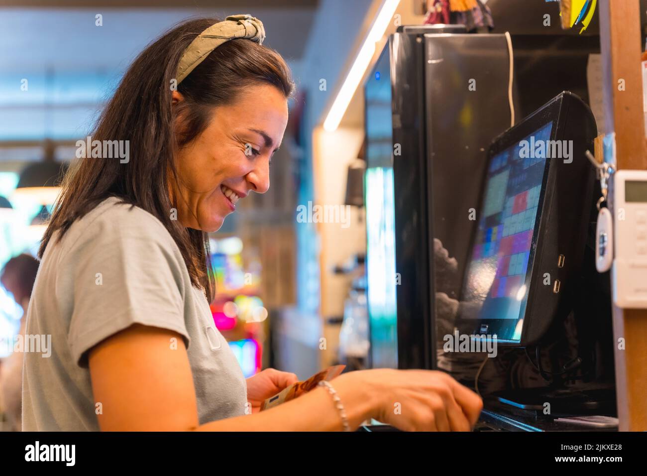 Brunette caucasian waitress smiling doing the check on the computer in ...