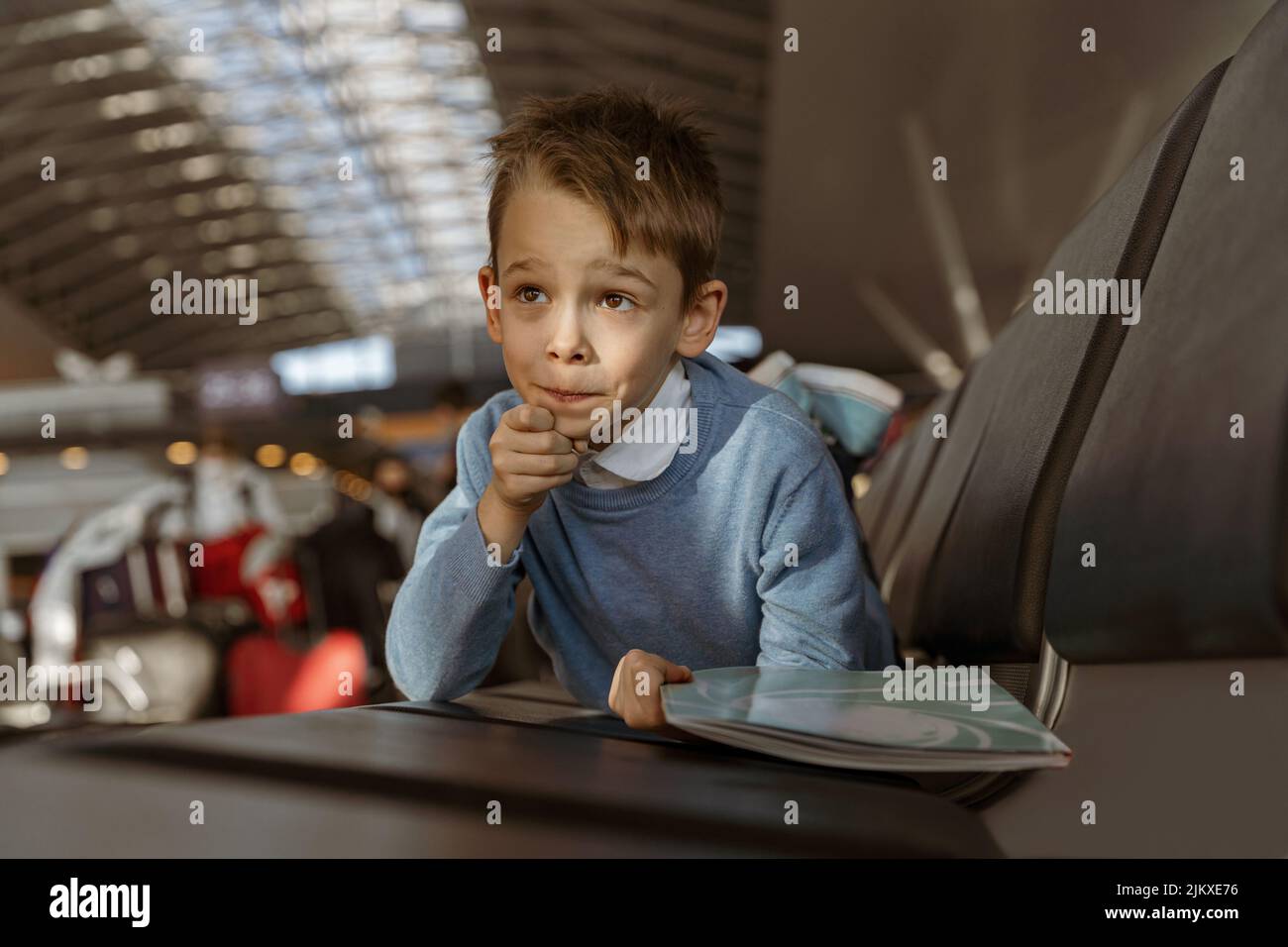 Little boy holding a book in the waiting room at the airport before the ...