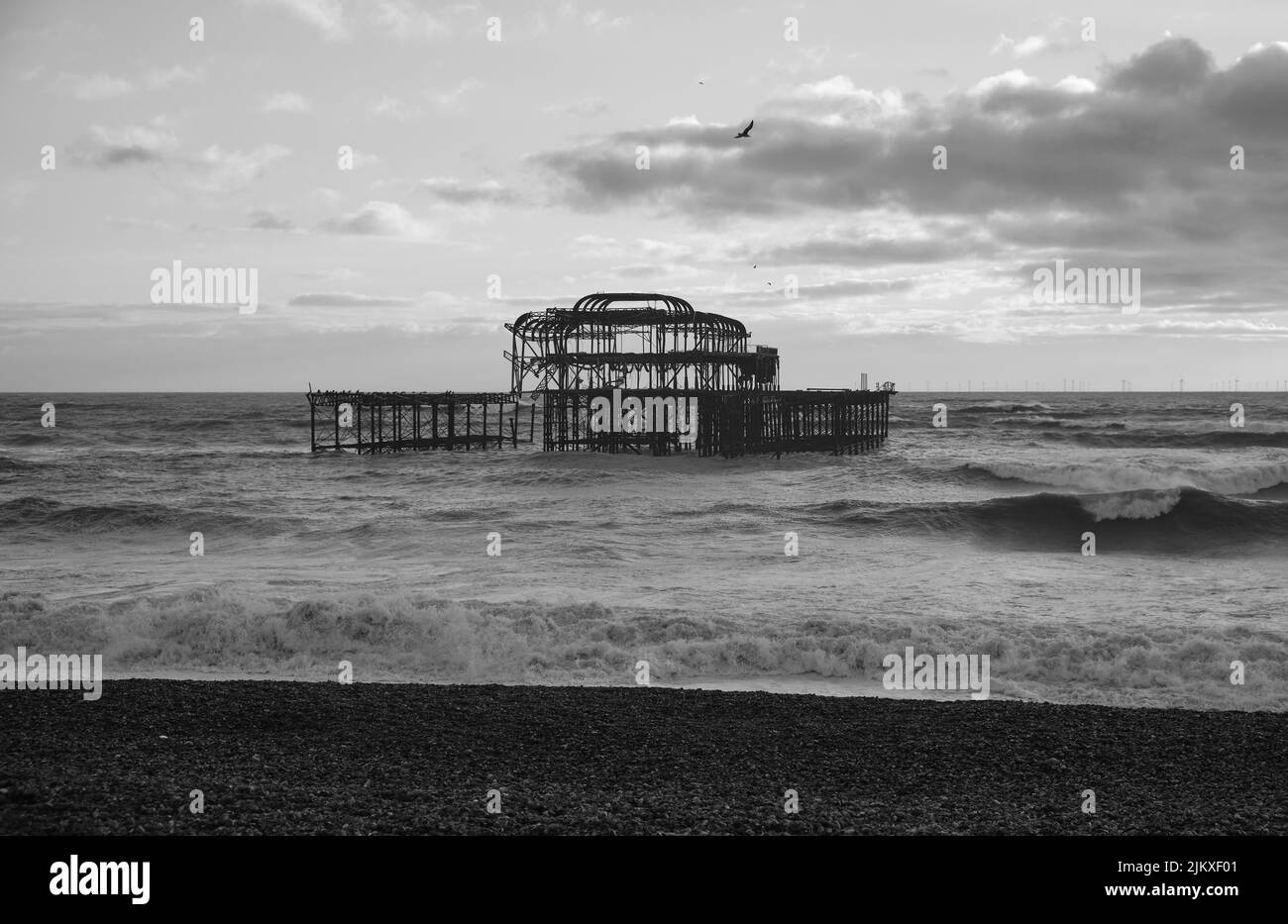 A grayscale view of the seaside and waves of Brighton with an old pier ...