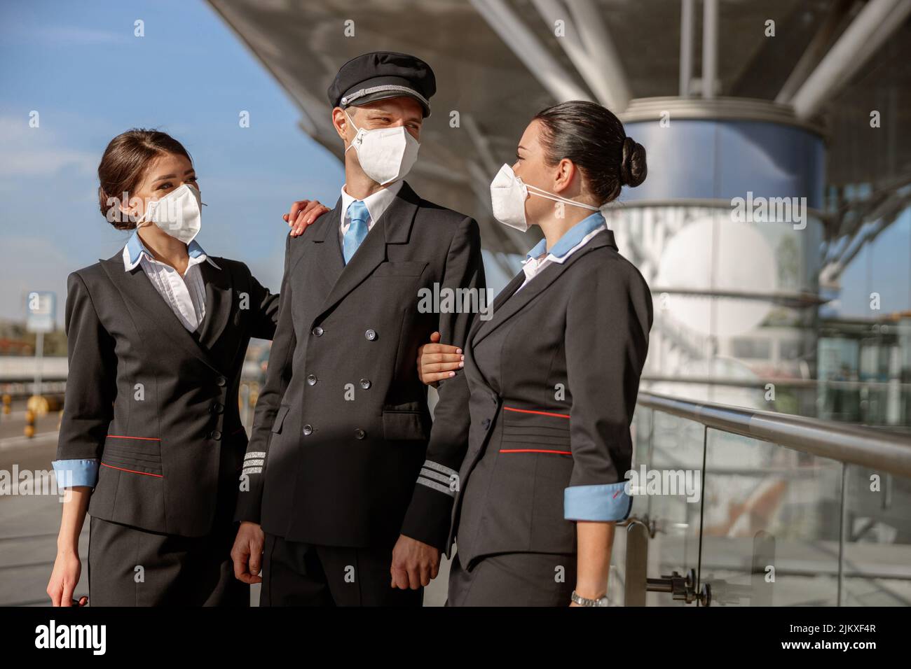 Pilot and two stewardesses wearing face masks and standing outdoor ...