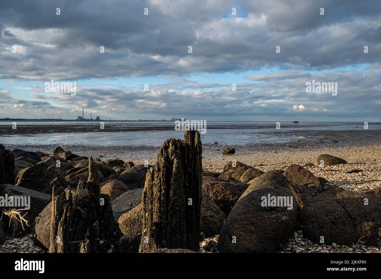 The rocky beach of Wadden sea under a cloudy sky, over a background of ...