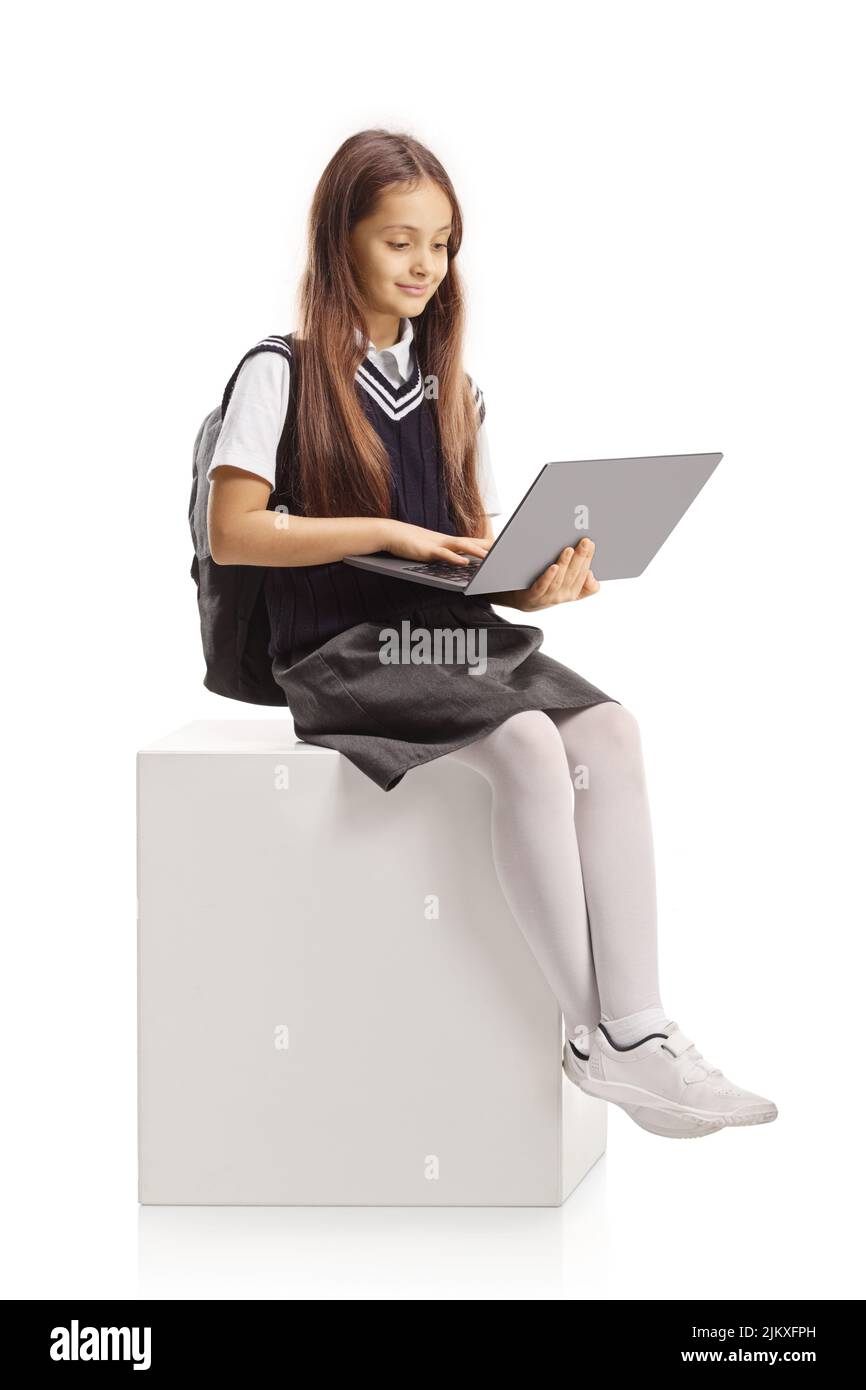 Girl in a school uniform sitting and using a laptop isolated on white ...
