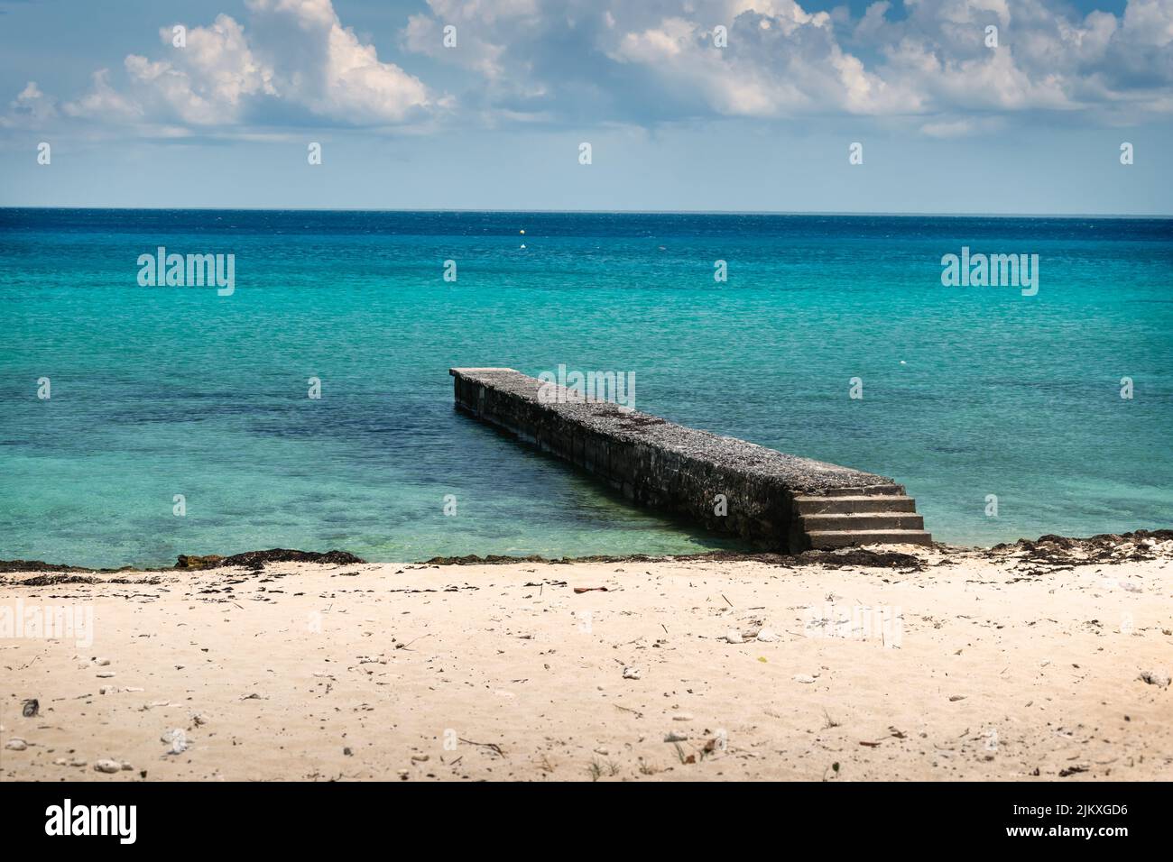 Small stone dock in a Caribbean beach with calm waters and a clear blue ...