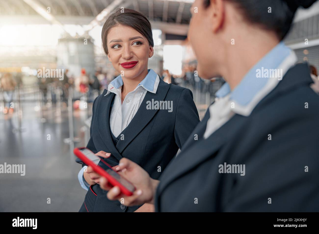 Two beautiful stewardesses using phones and talking in the airport ...