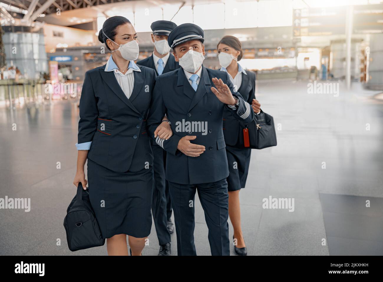 Male pilots and female flight attendants walking in airport terminal ...