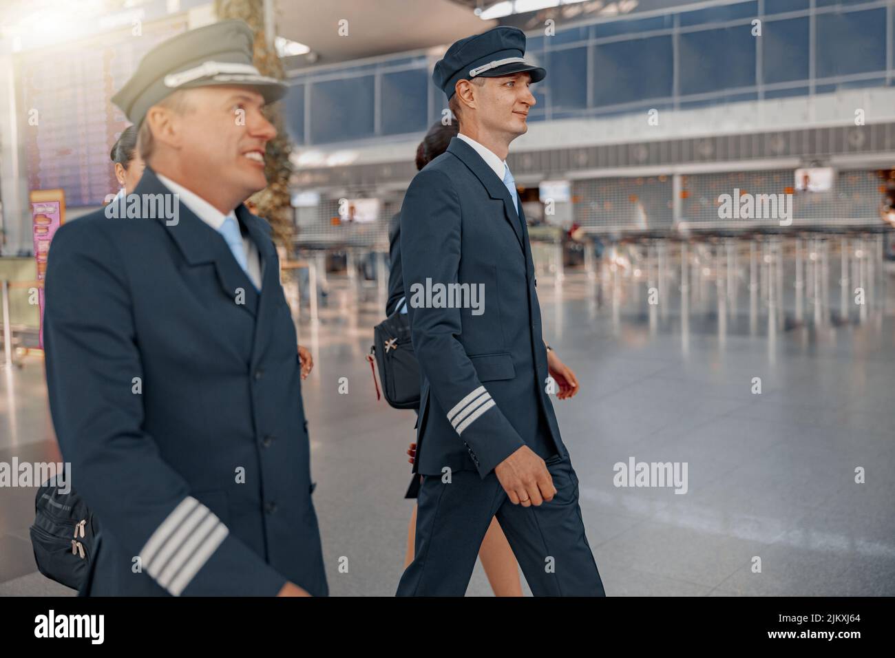 Smiling male pilots walking along the airport terminal Stock Photo - Alamy