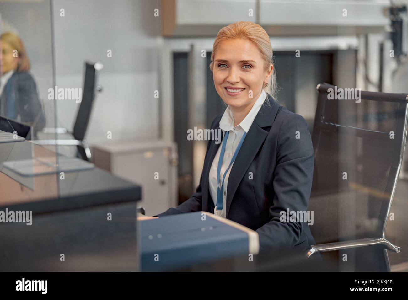 Smiling pretty female airport employee sitting at the check-in desk ...