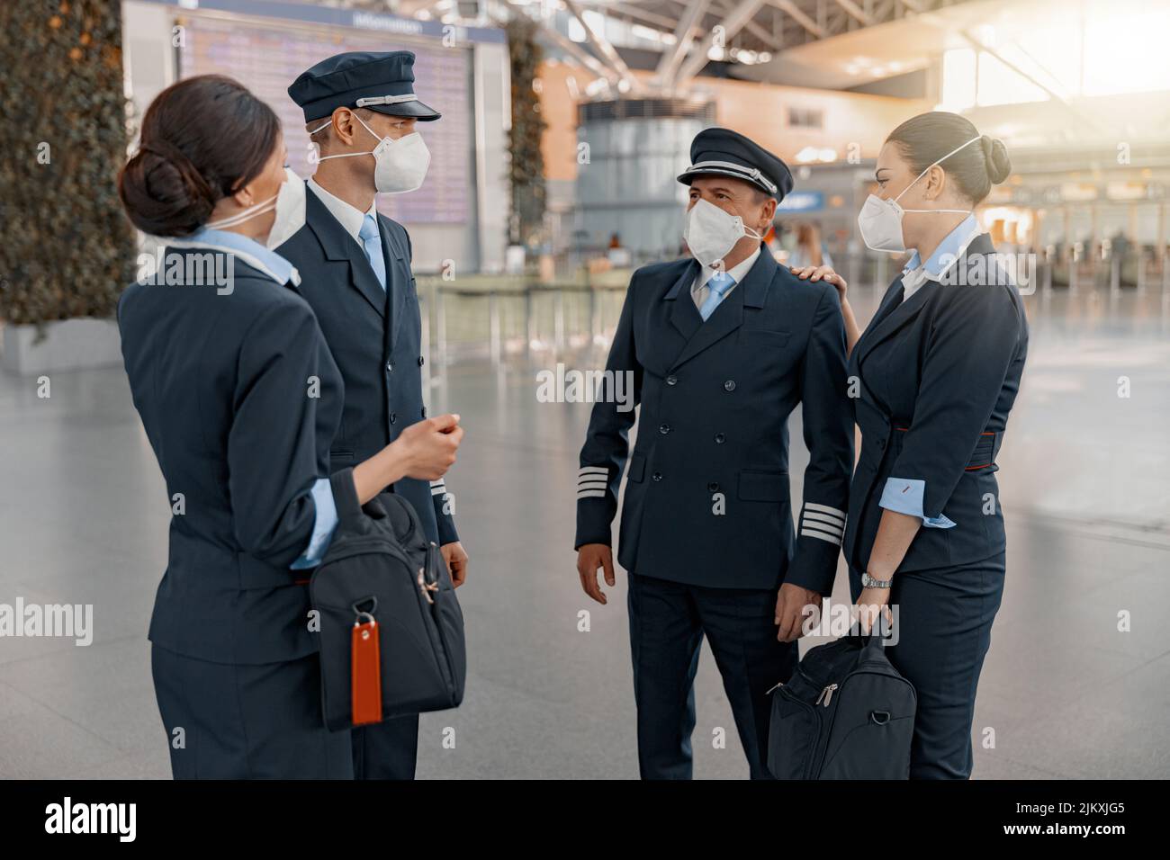 Male pilots and female flight attendants talking in airport terminal ...