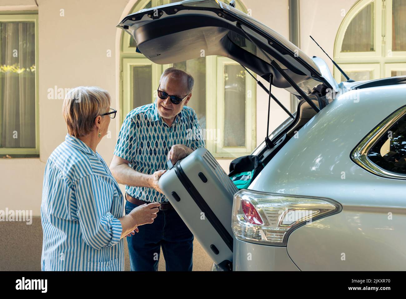 Elderly couple loading trolley in car trunk, travelling on retirement ...