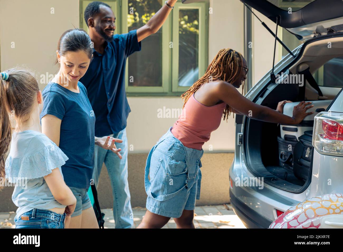 Diverse people loading luggage in trunk of automobile, travelling on ...