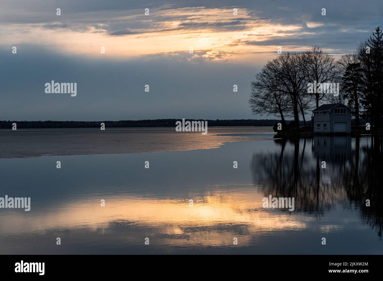 A beautiful shot of big leafless trees and rural house at lakeshore ...