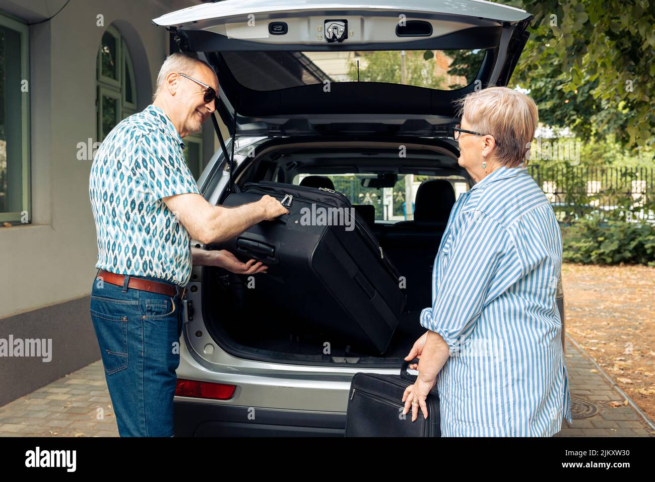 Aged couple putting bags in vehicle trunk to leave on retirement ...