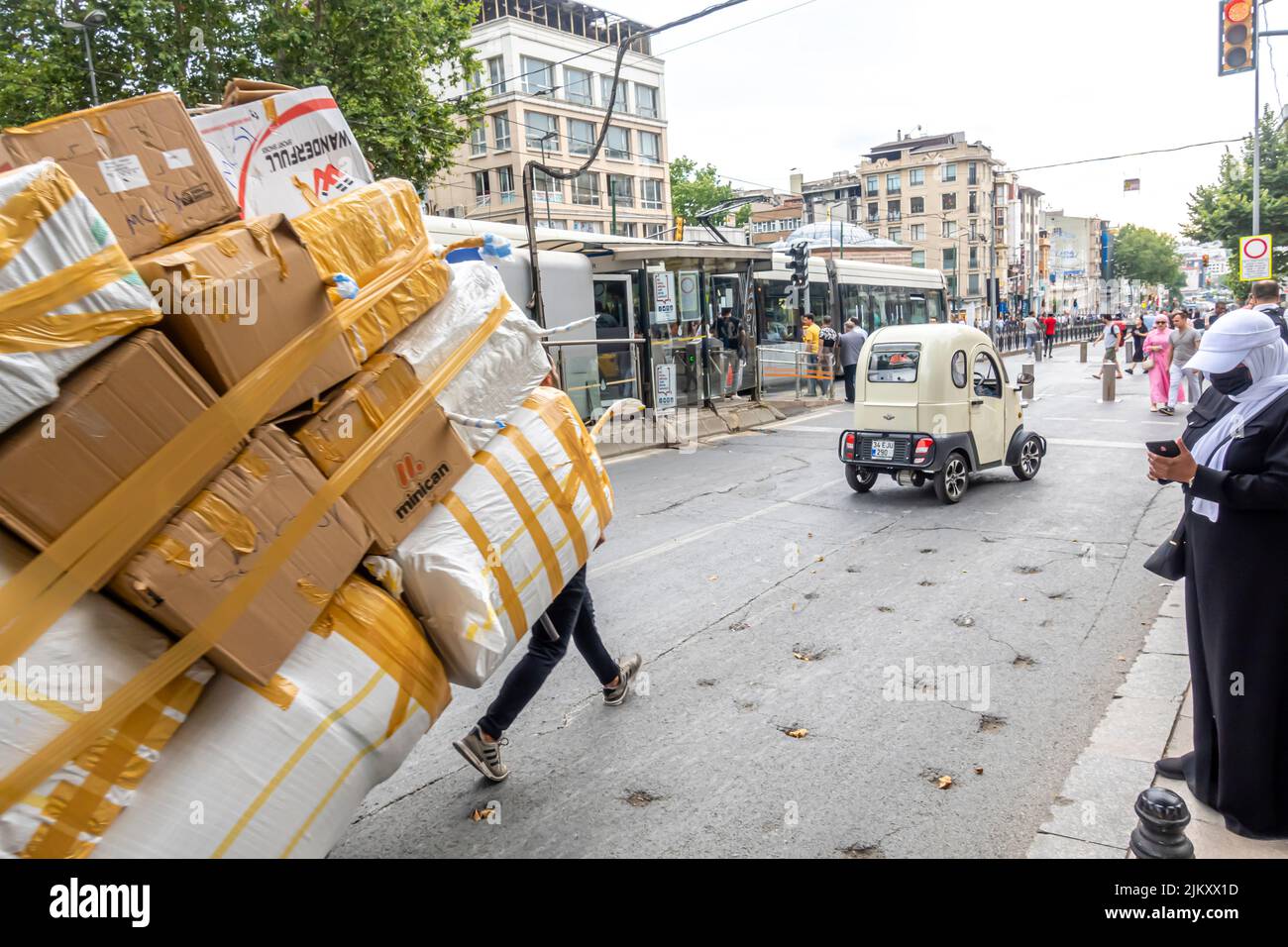 A teenager worker dragging large hand-pulled cart with wrapped boxes ...