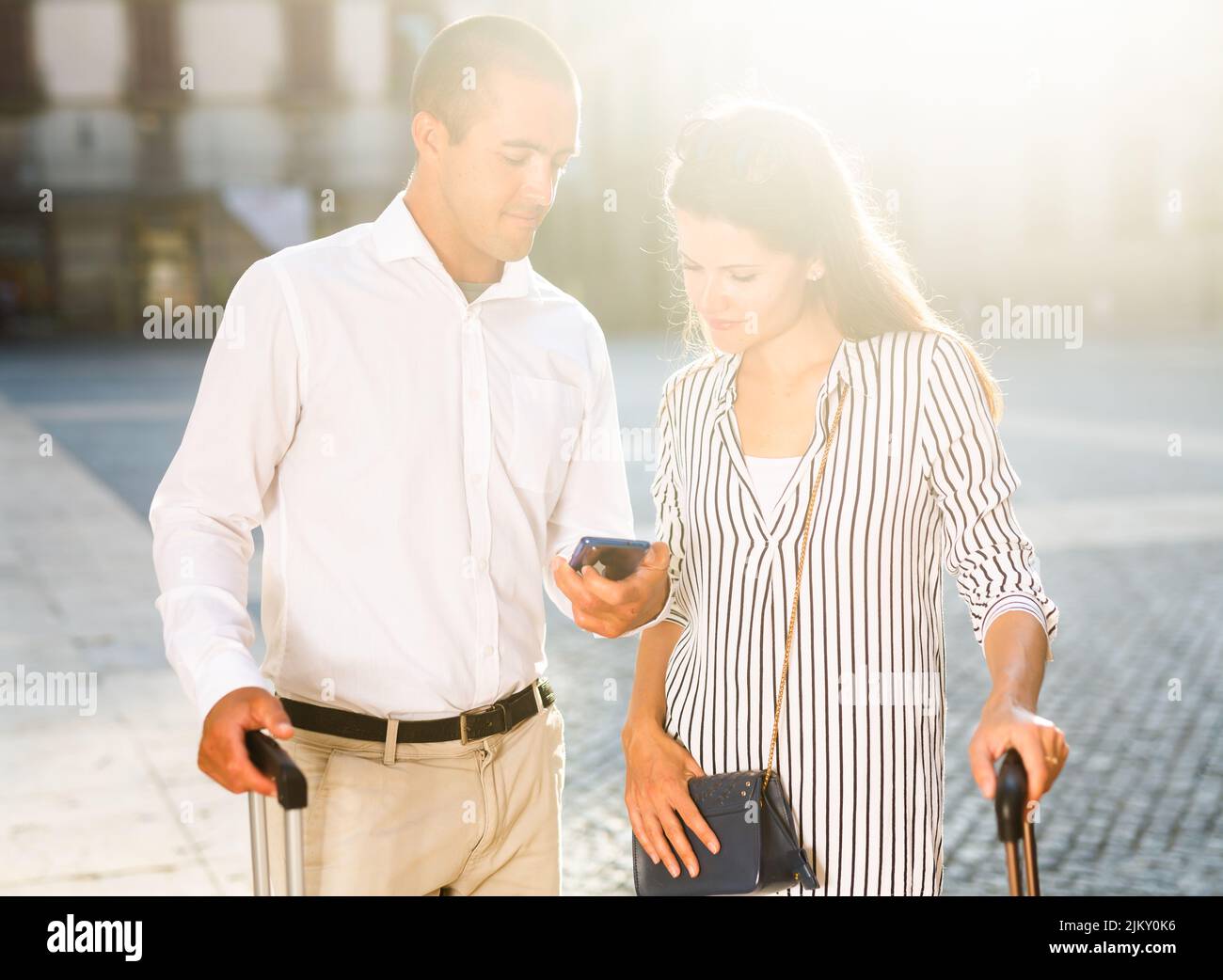 Couple of tourists walking with suitcases, looking at map in cellphone ...