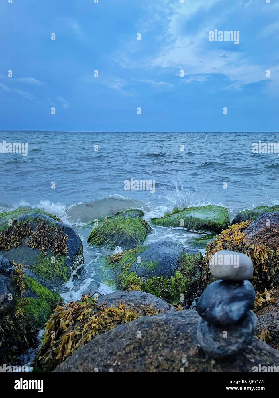 A vertical shot of the waves hitting the rocky shore on a gloomy day ...