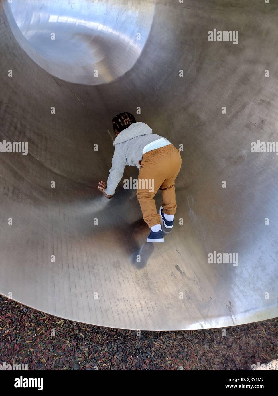 A vertical shot of a small kid from behind climbing inside the metal ...