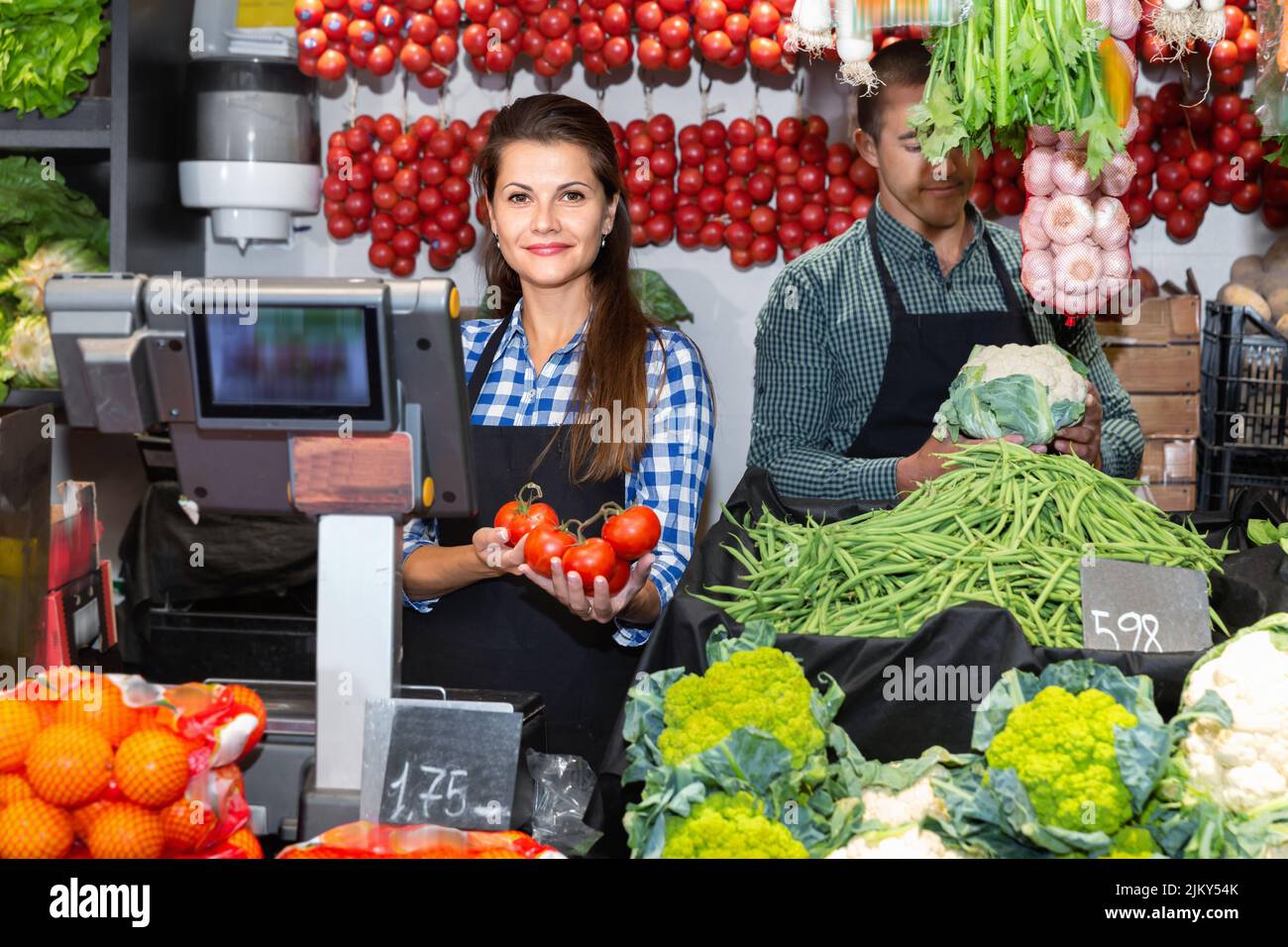 Portrait of female and male vegetable shop assistants laying out and weighing vegetables on ...