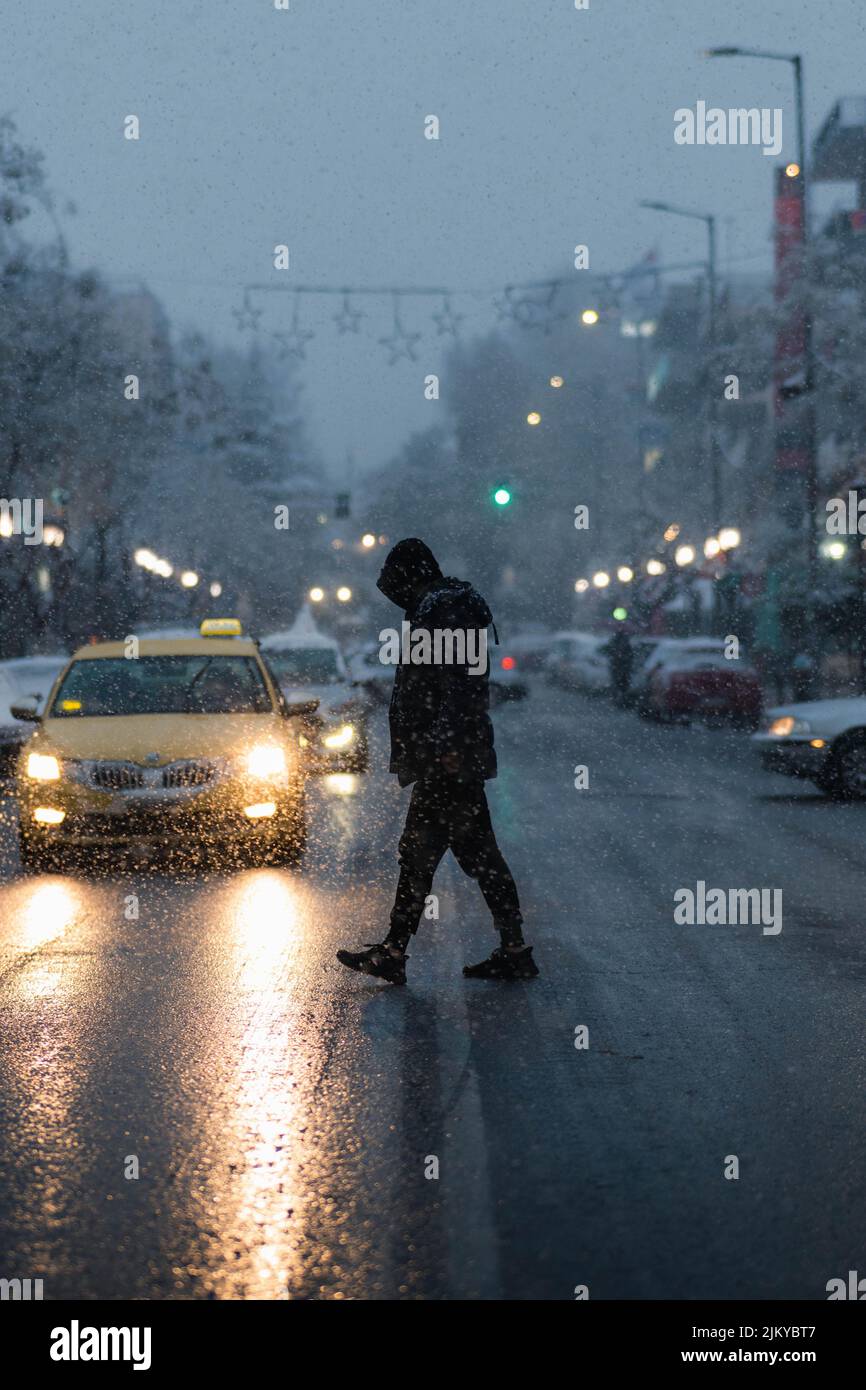 A vertical shot of a man with hoody crossing the road while it is ...