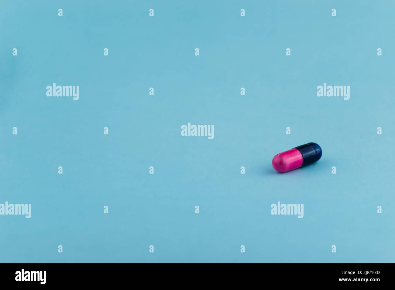A pink and black pill on a light blue surface. Medical supplies Stock ...