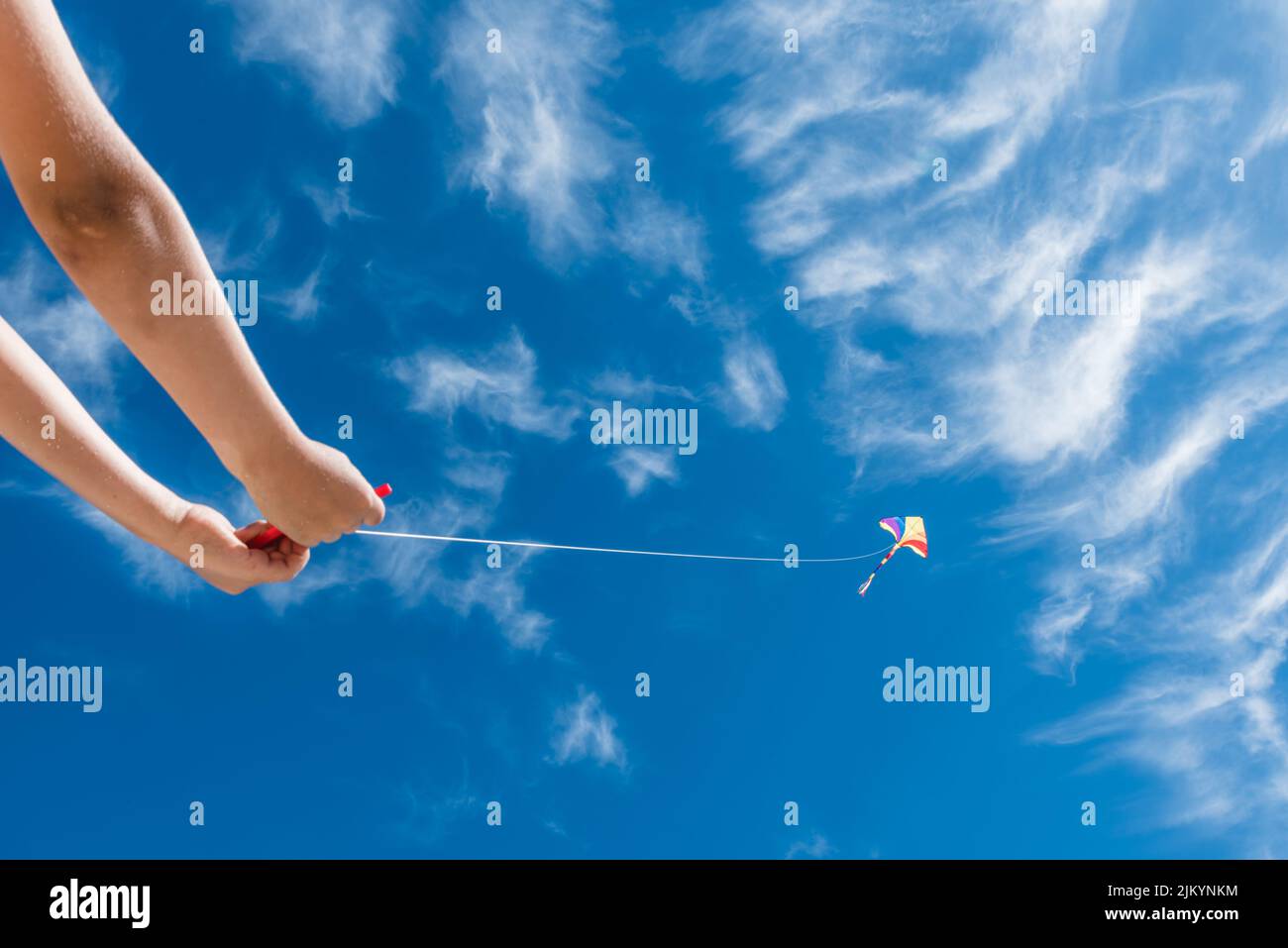 A low angle shot of someone holding the rope of a rainbow flying kite ...