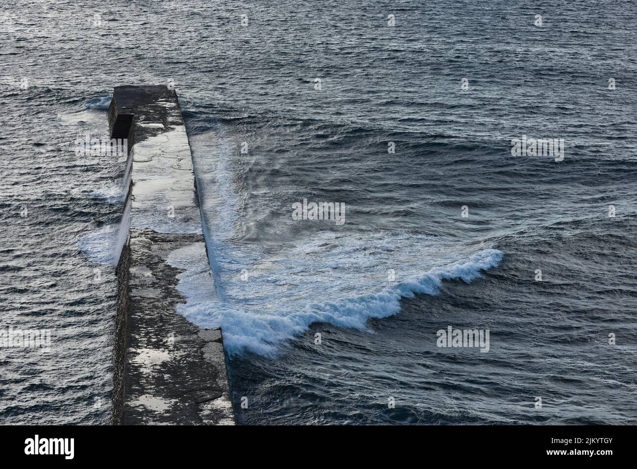 A high angle shot of a concrete breakwater on the beach with splashing ...