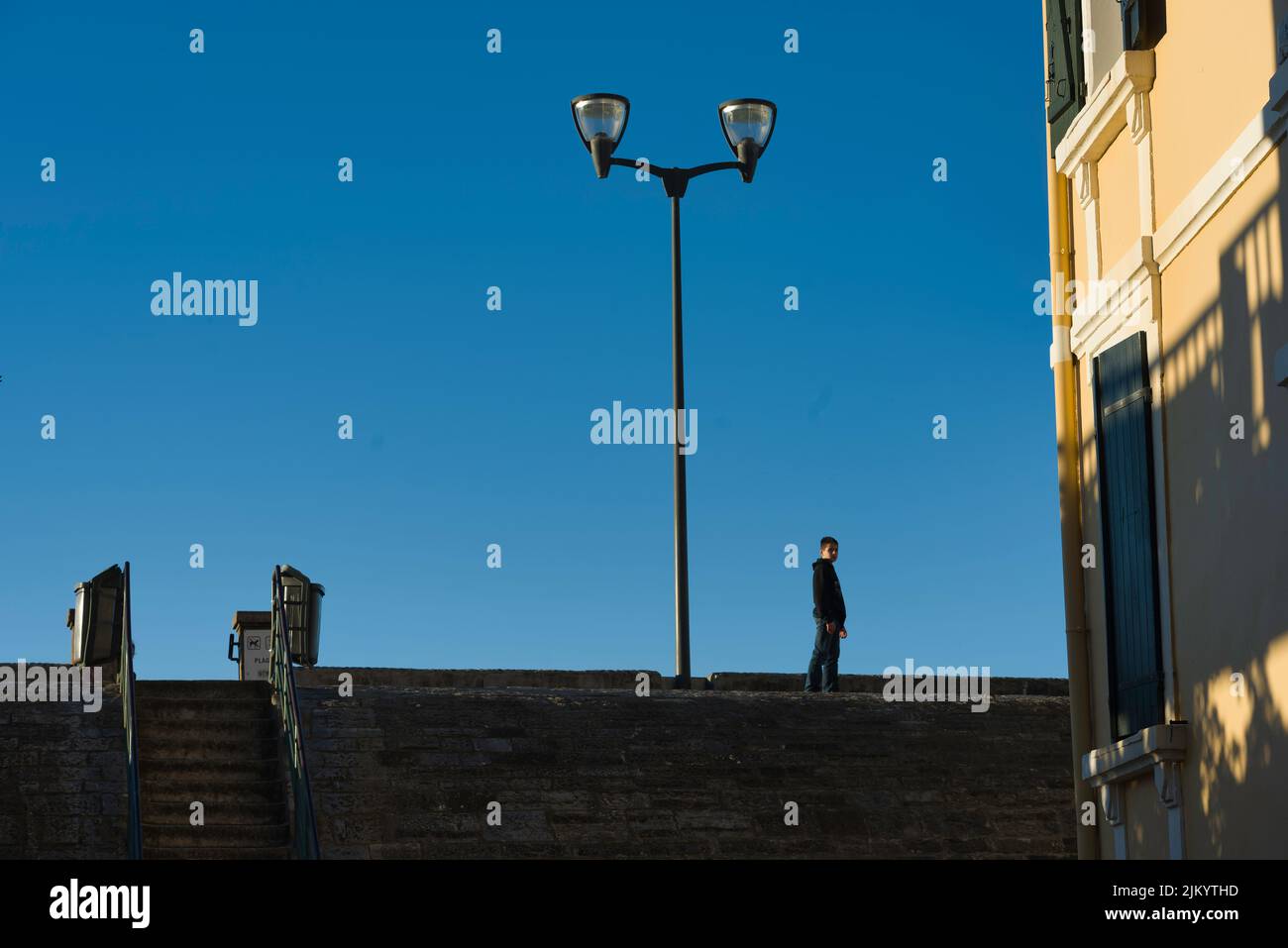 A male standing next to a tall outdoor lamps on a concrete elevation ...