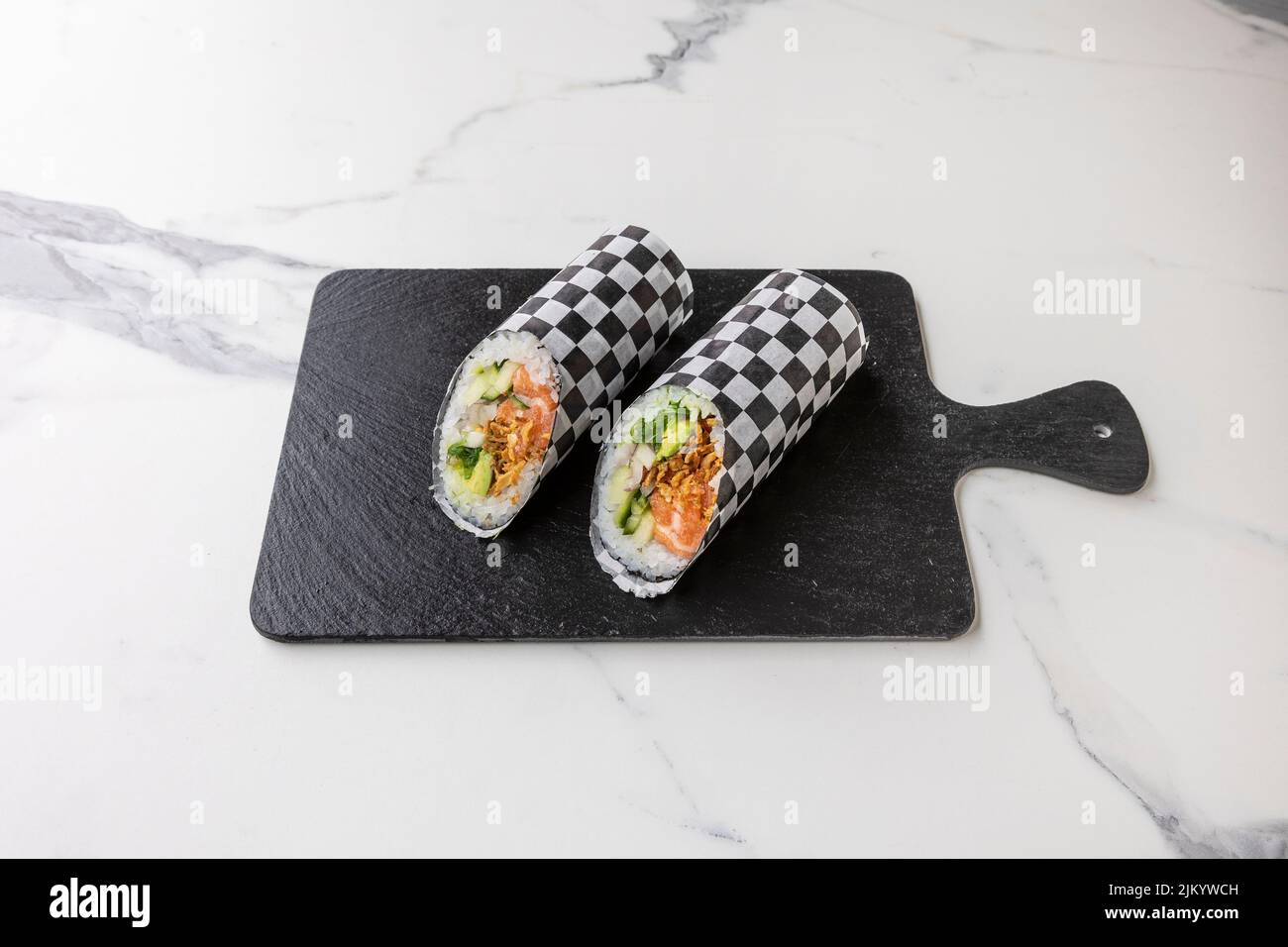 A closeup shot of sushi roll in black and white wrapper on a dark board ...