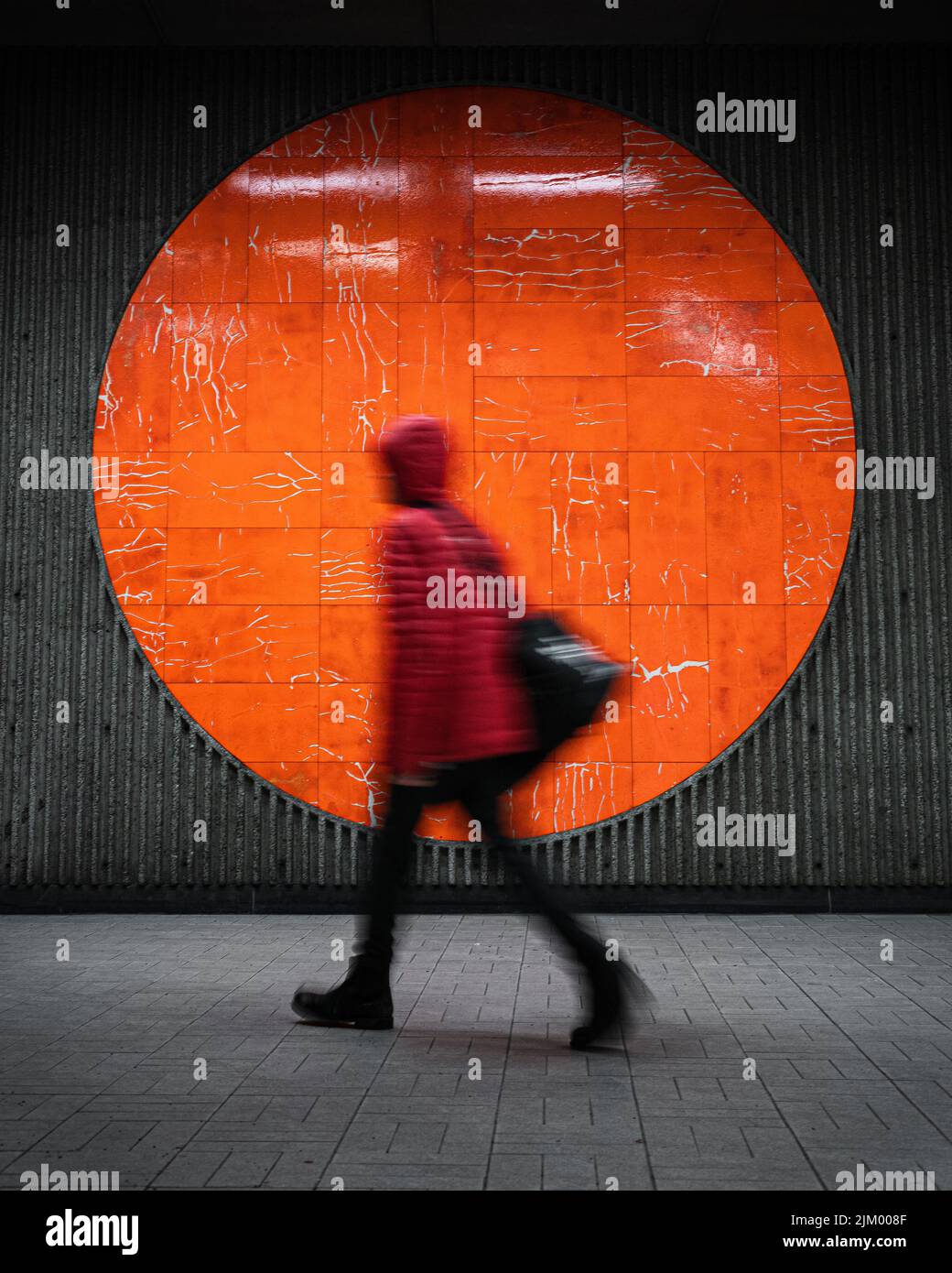 A vertical shot of a person walking near an orange circular mural in a ...