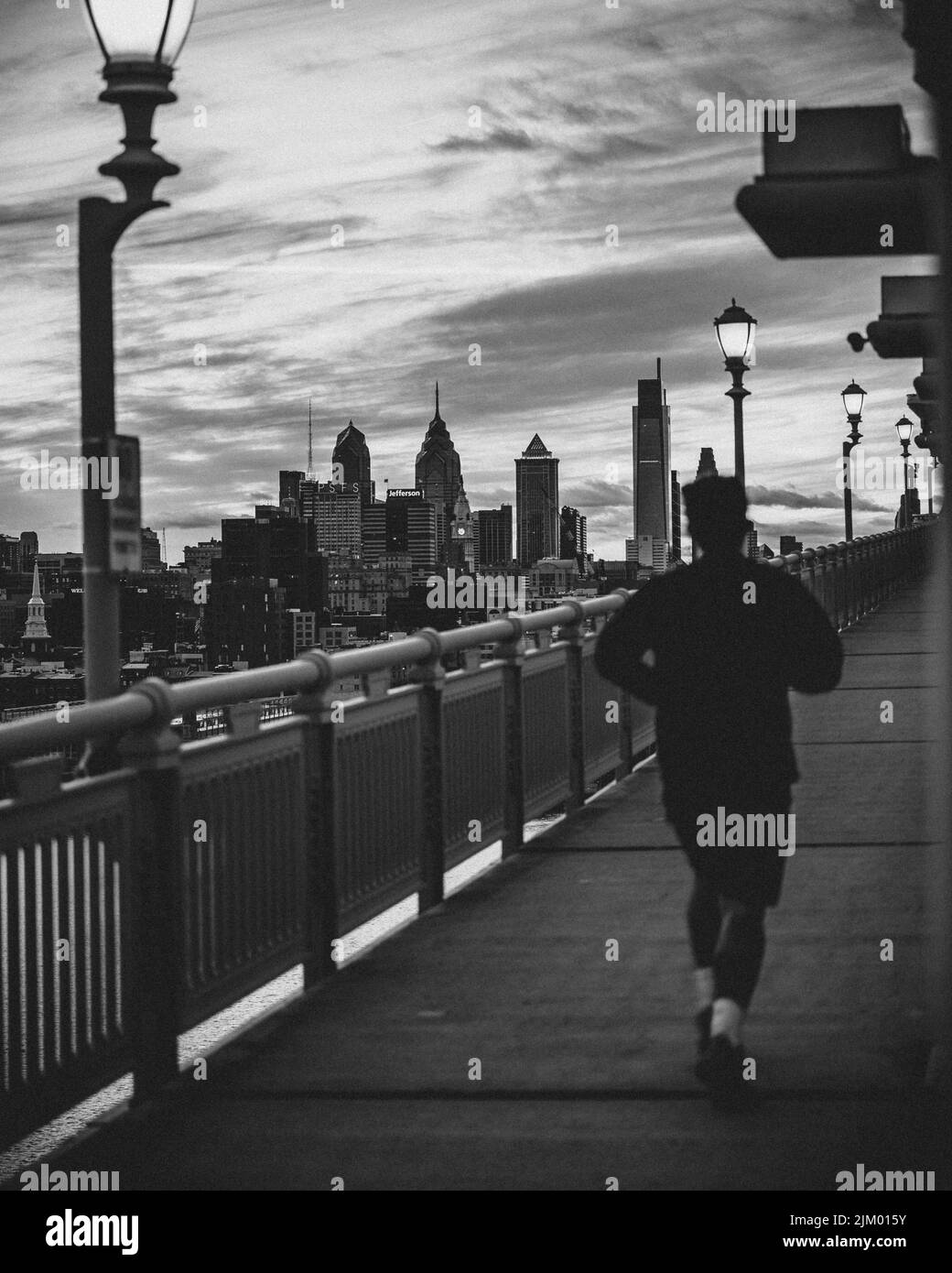 A vertical grayscale back view of a man jogging in the street with ...