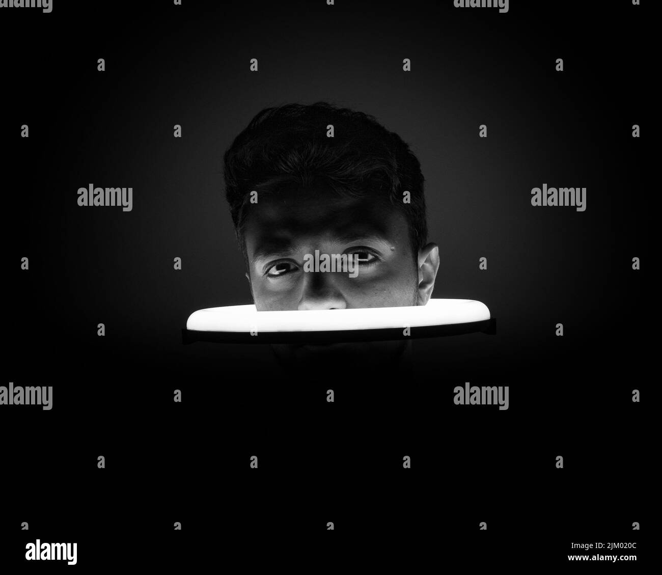 A portrait of a South Asian man peeking eyes through a ring light in ...