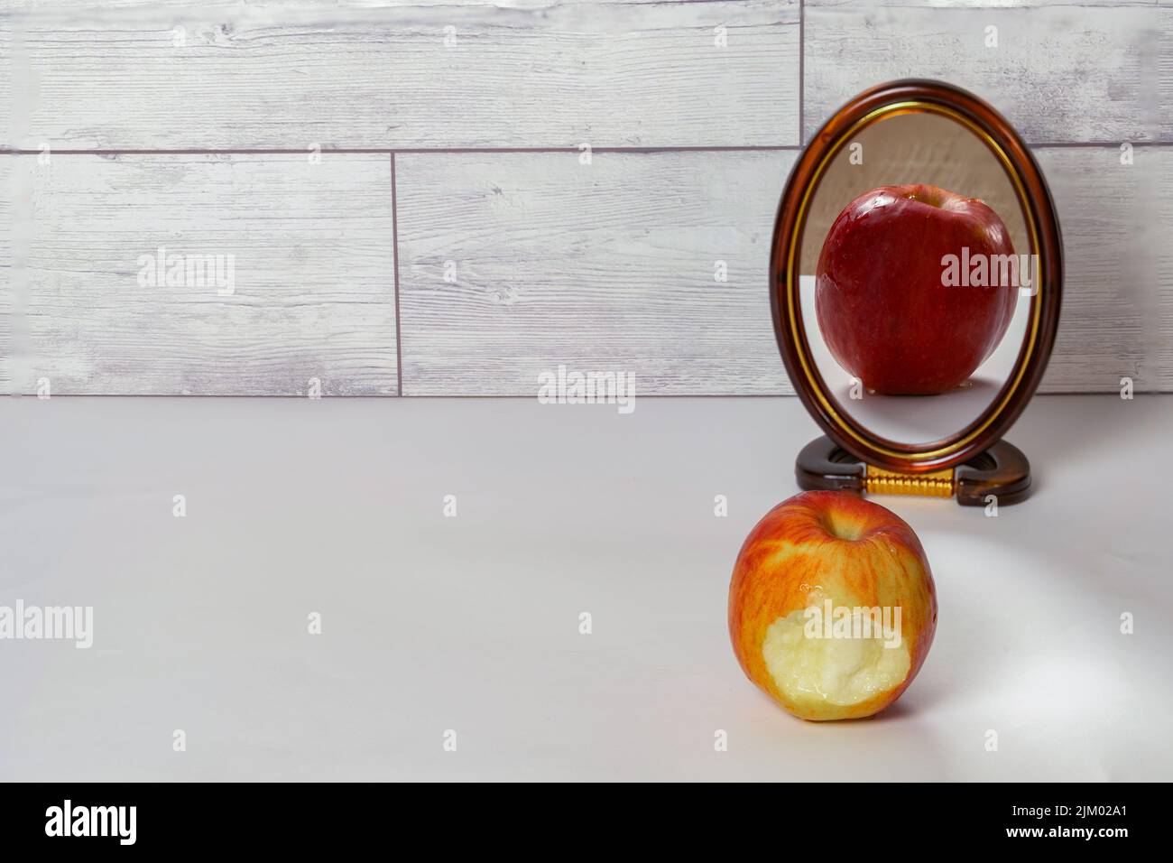 bitten red apple reflected in a mirror isolated on a white table with ...