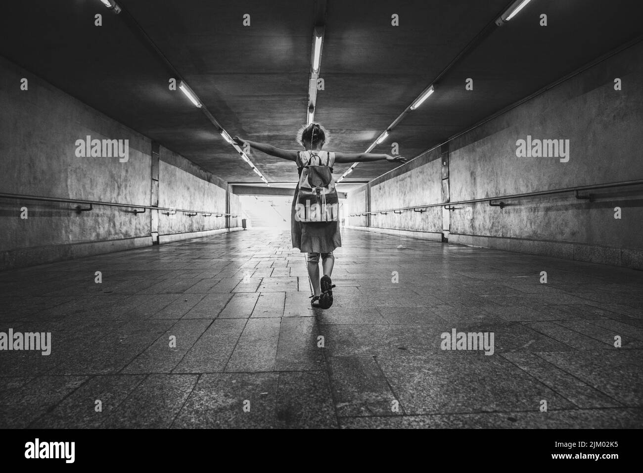 A black and white shot of a little girl walking in an underpass tunnel ...