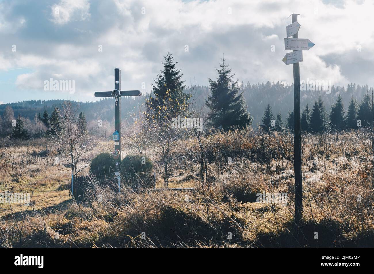 An old cross and a pole with direction signs in a rural area in cloudy ...