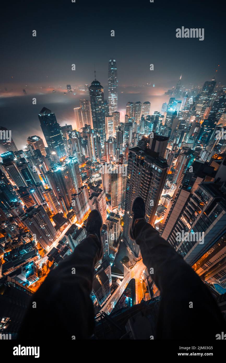 A vertical futuristic cityscape at night with a daring man dangling his ...