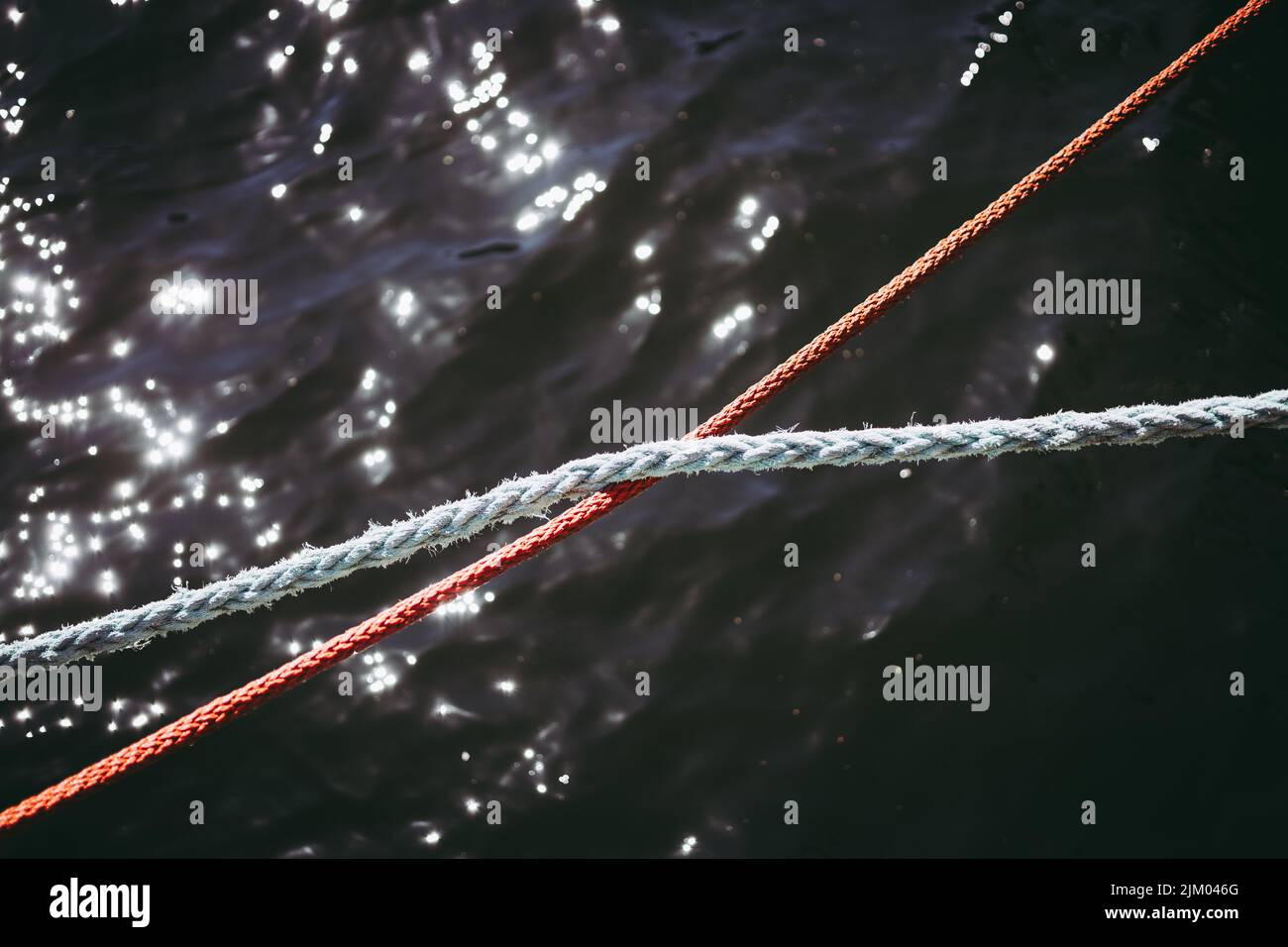 A closeup of red and blue crossing ropes above water reflecting the ...