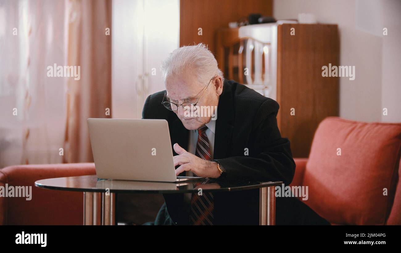 An old man in glasses typing something in a laptop Stock Photo - Alamy