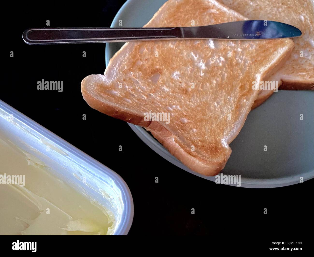 A closeup of toast with a tub of butter next to it and a knife on top ...